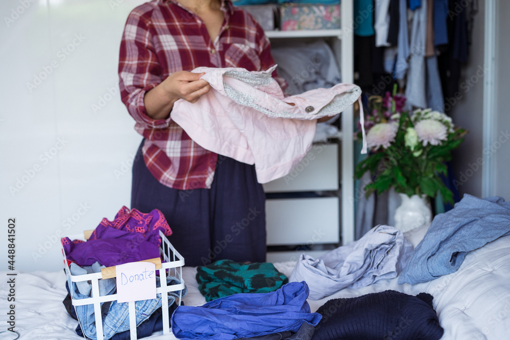 A Woman selecting clothes from her wardrobe for donating to a Charity ...
