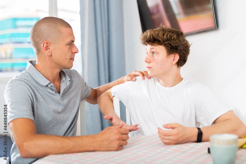 Portrait of teen boy having conversation with man in home interior ...