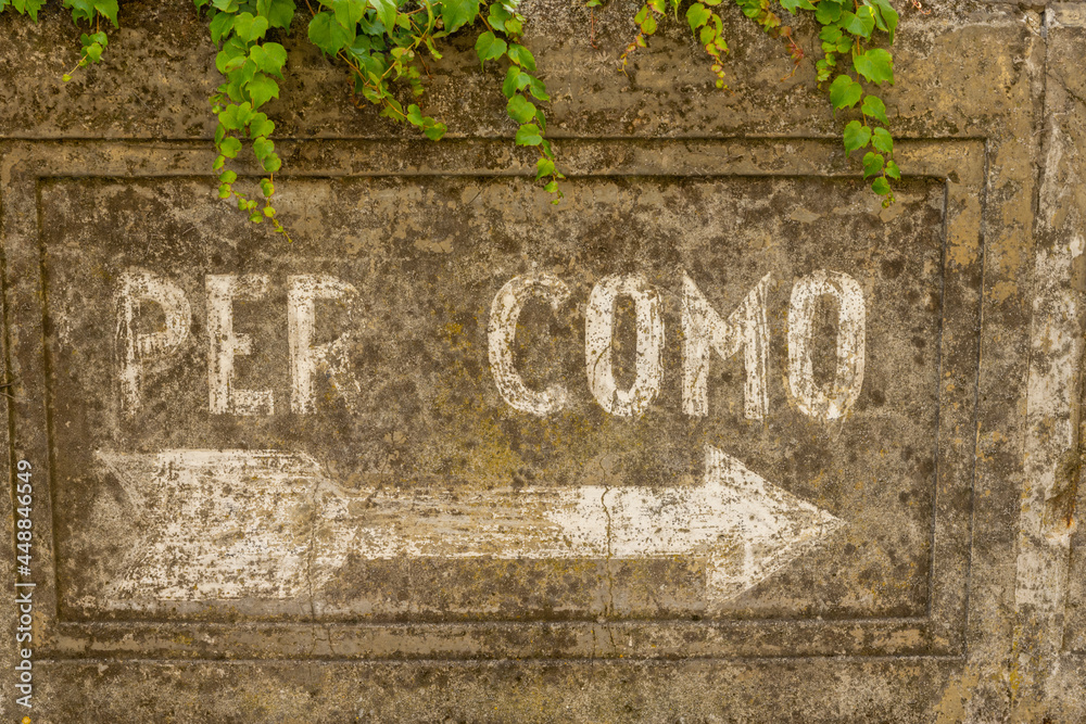 Old painted sign on a wall, showing direction to the city of Como ...