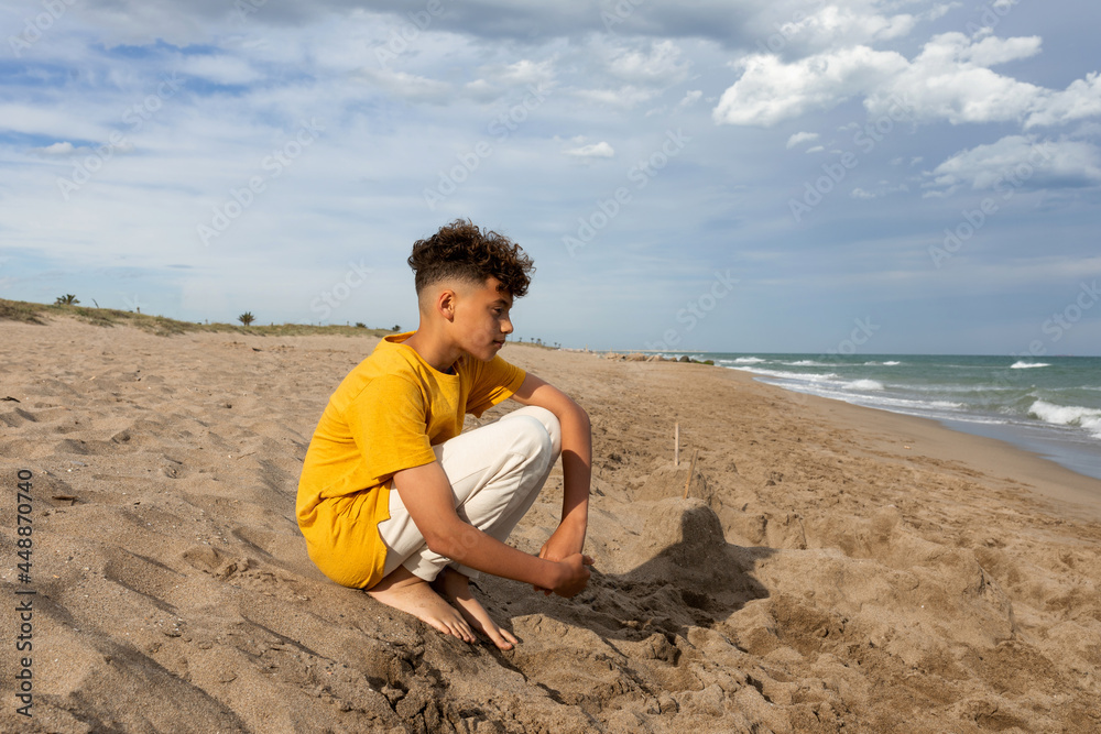 Teen boy sitting on the sand at the beach Stock Photo | Adobe Stock