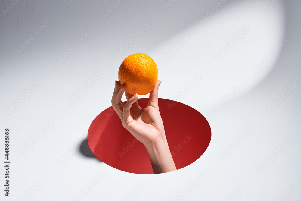 Woman's hand holding orange fruit on index finger through a hole cut in ...