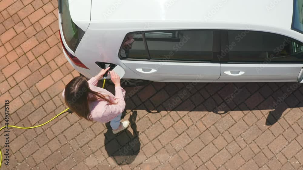 Overhead shot of a young Caucasian woman on the electric cars charge ...