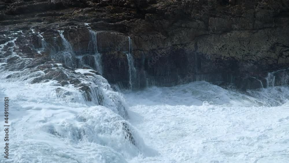 Wave crash into rocks, frothing sea water streams down rock-face ...