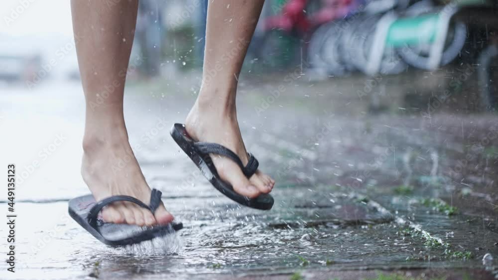 Low angle shot feet in flip flops stomping on water puddle on rainy day ...