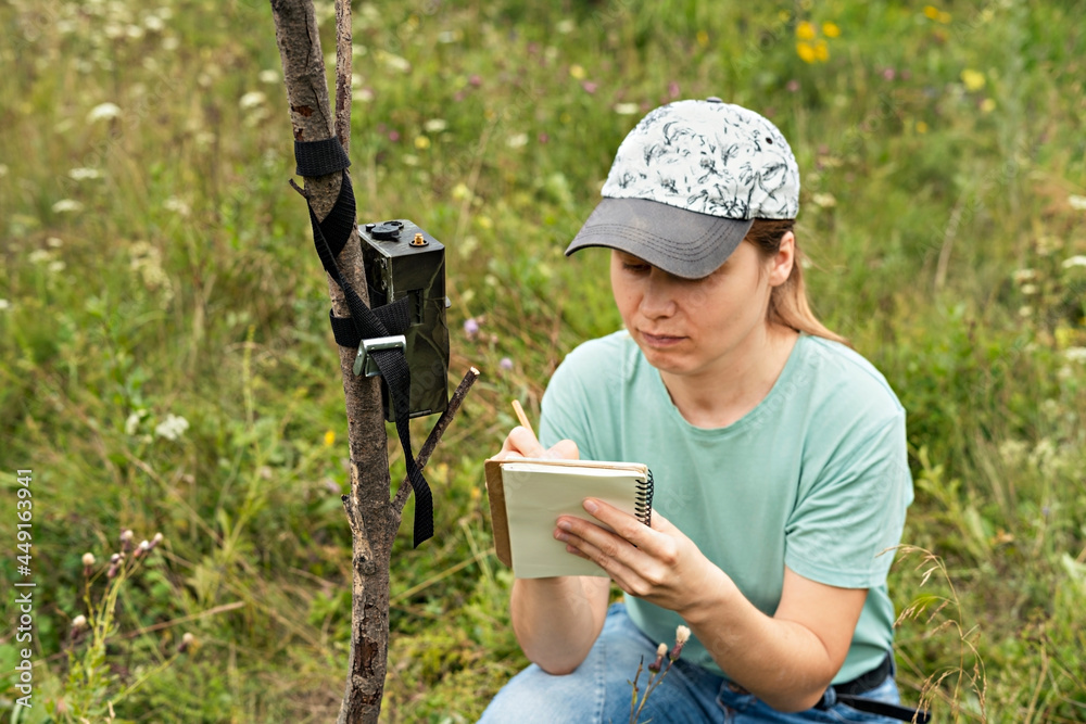 Young woman scientist zoologist writing down data from trap camera to ...