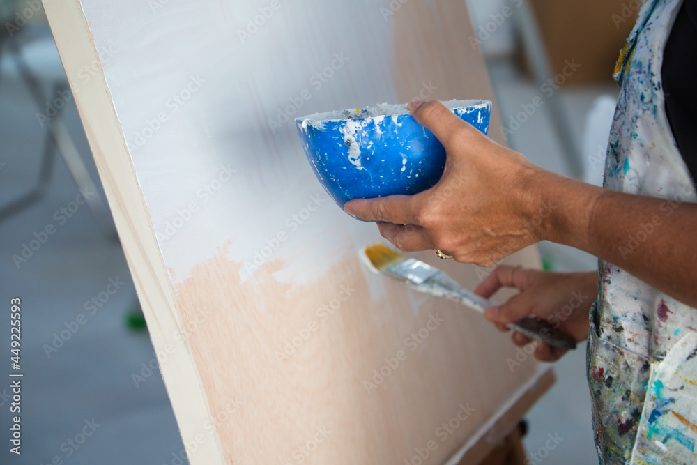 Mature woman with glasses is painting a white background. The woman is ...