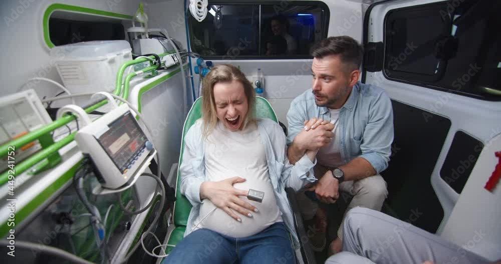 Caucasian young husband supporting pregnant wife in ambulance car ...