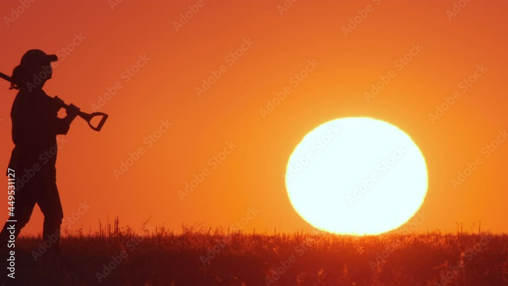 Silhouette man farmer or gardener walks across field with shovel on ...