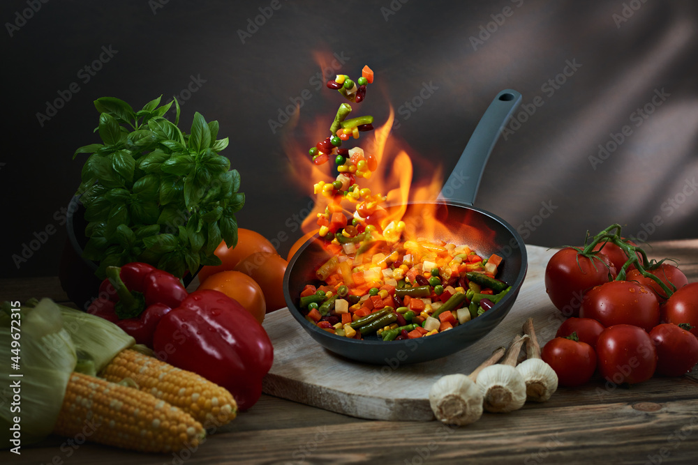 Assorted fried vegetables in a pan with a flame of fire. Flambe ...