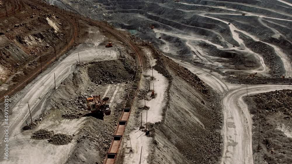 Large excavator loads rock formation to the freight train. Mining work ...