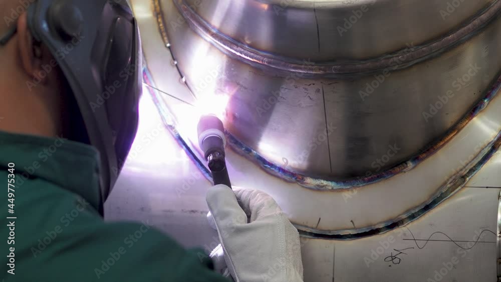 Skilled welder using TIG welding machine inside workshop, wearing mask ...