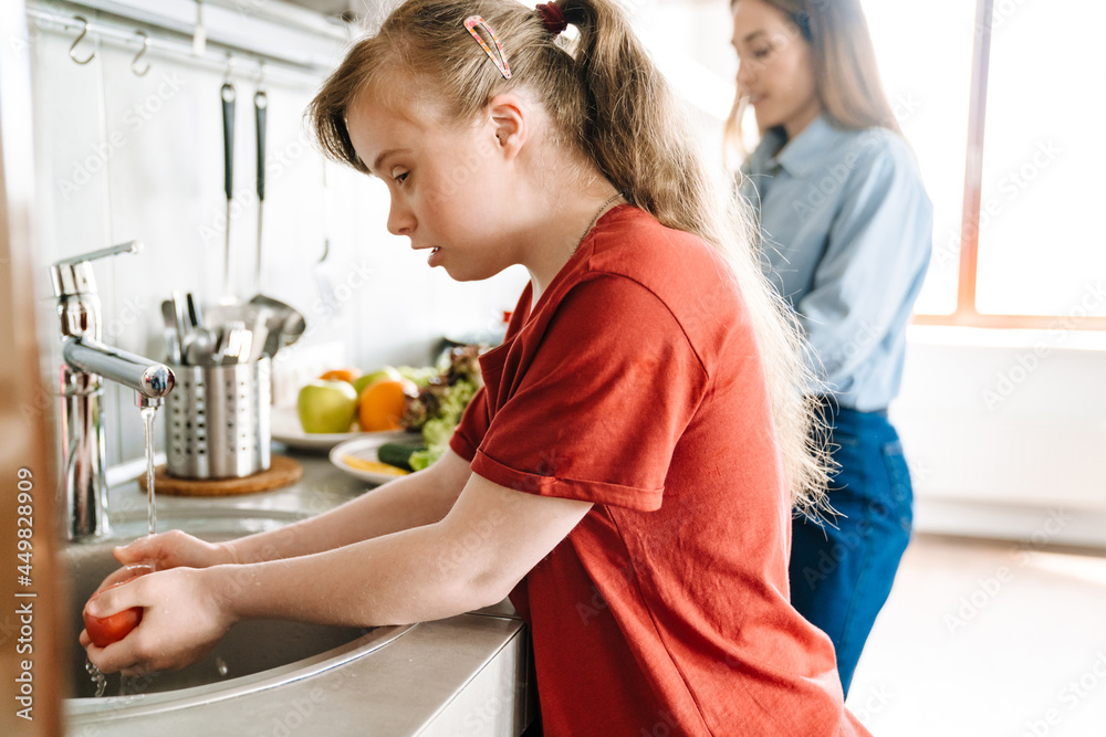 White woman and her daughter with down syndrome cooking in kitchen ...