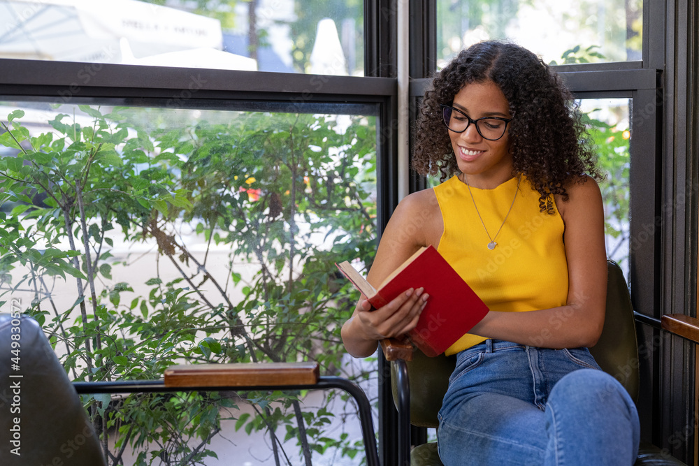 young beautiful african woman in a library reading a book in total ...