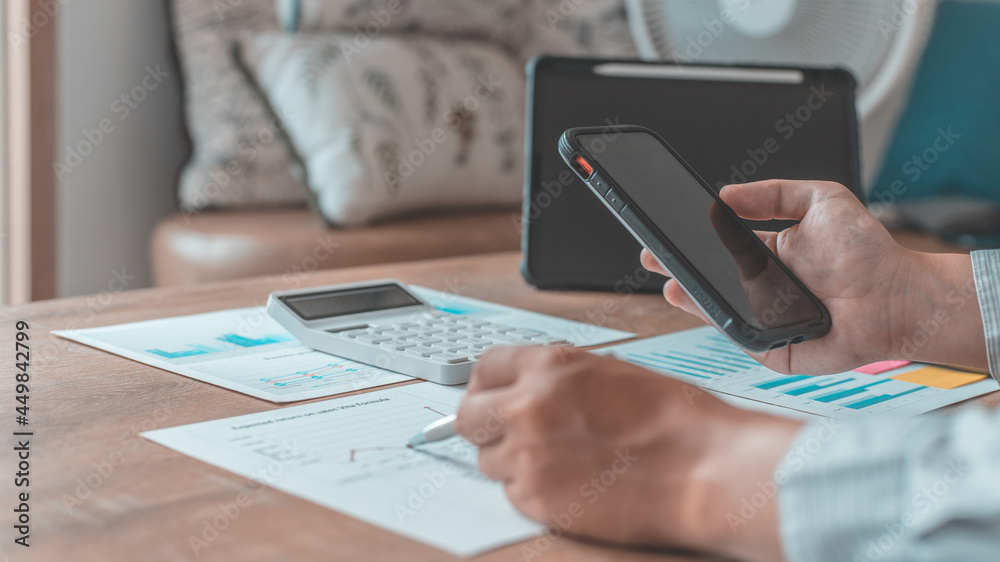 Businessman uses a mobile phone to examine financial data and analyze ...