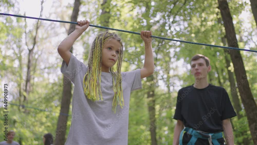Active child fearlessly climbs the ropes between the trees. Girl in an ...