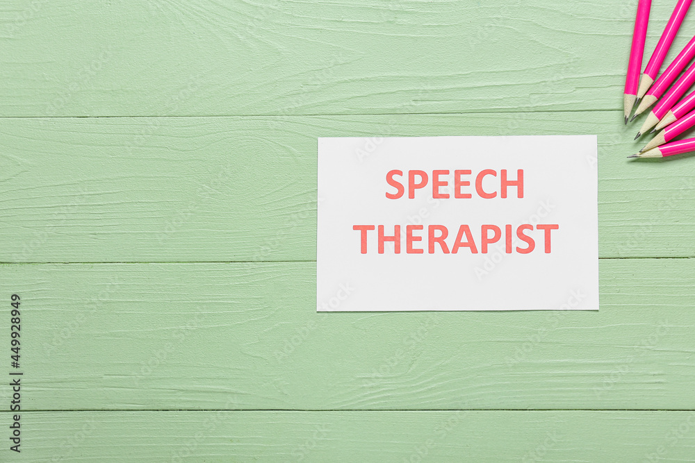 Paper with text SPEECH THERAPIST and pencils on color wooden background ...