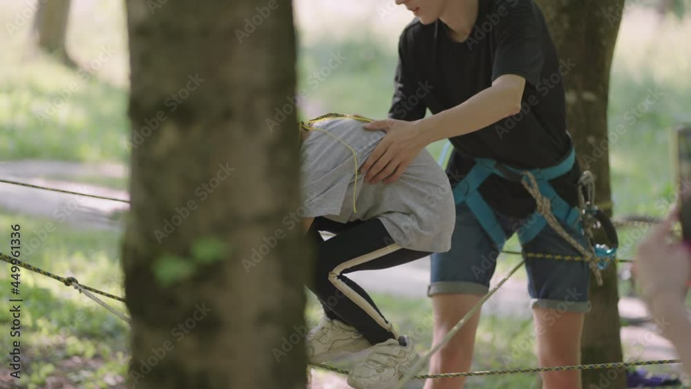Active child fearlessly climbs the ropes between the trees. Girl in an ...