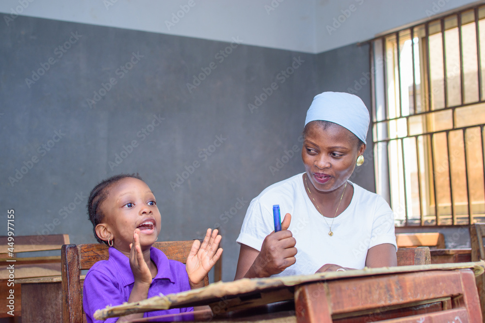 African Nigerian mother or teacher sitting together with her girl child ...