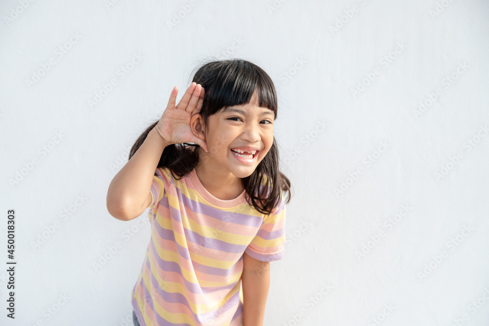 Little Asian girl holds her hand near her ear and listenings ...