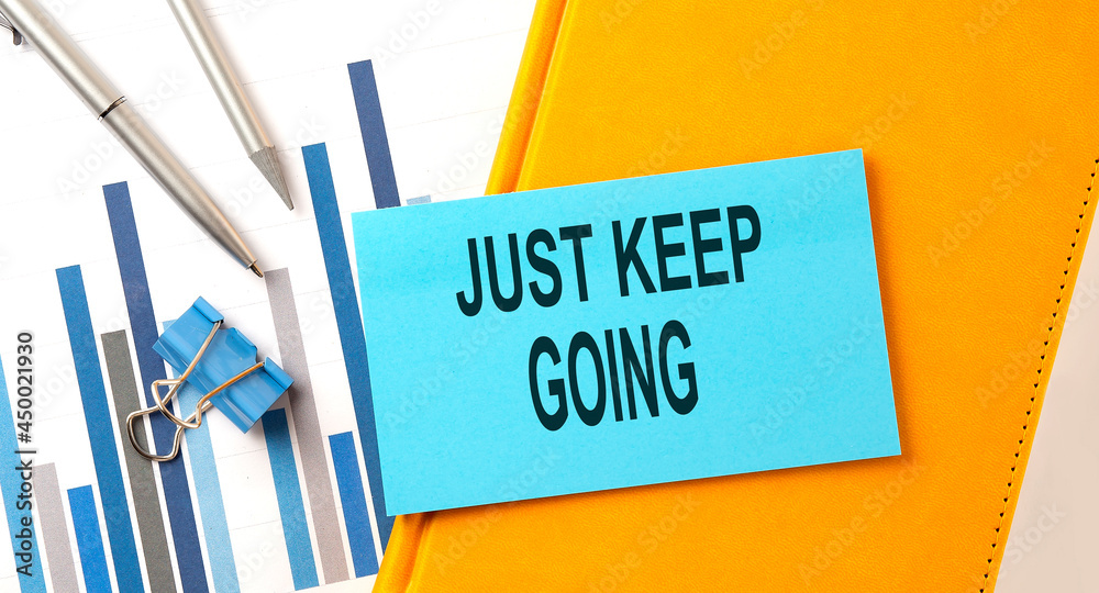 JUST KEEP GOING text on sticker on the yellow notebook with chart and ...