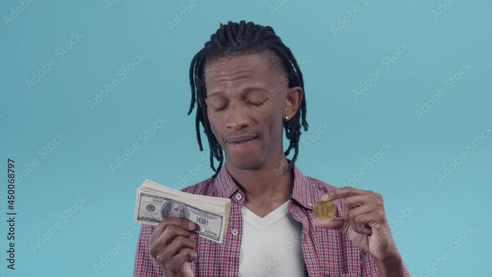 Black man with dreadlocks looks at a pack of dollar bills and a gold ...