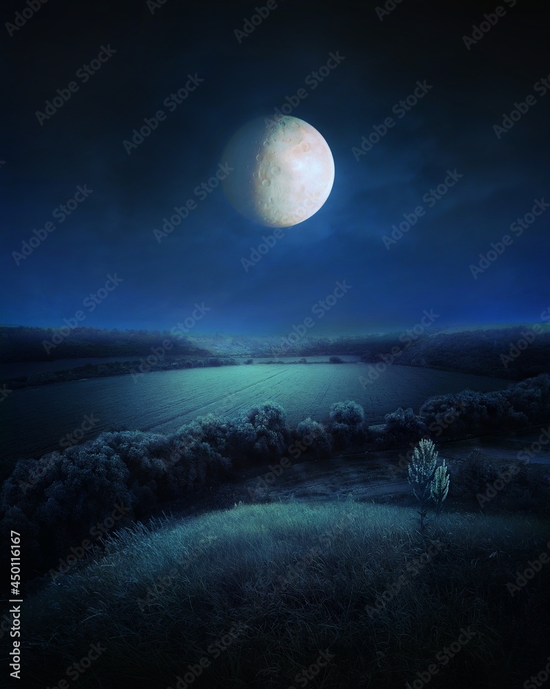 Big moon in the night sky over green hills and fields. Bright light ...