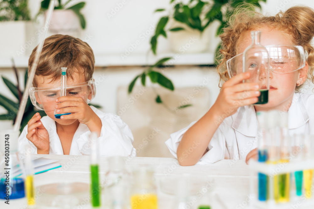 Serious little boy and girl in white uniforms conducting chemical ...