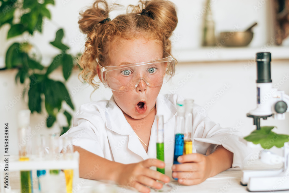 Surprised little red-haired girl in white uniform conducting chemical ...