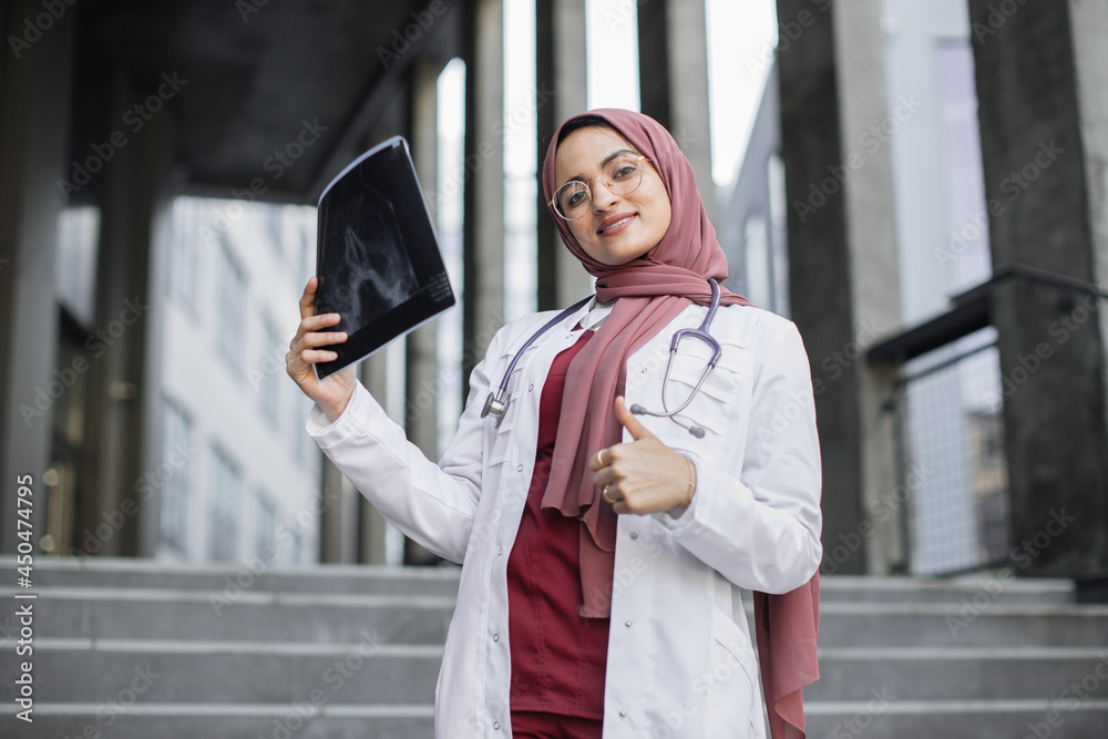 Attractive happy Muslim female doctor in hijab, examining an x-ray of ...