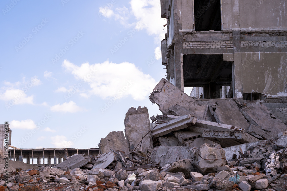 A ruined large building with a pile of gray concrete fragments of slabs ...