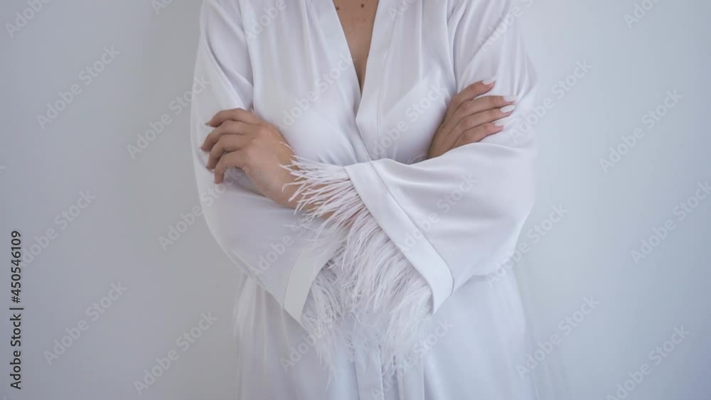 Caucasian bride in a satin robe with feathers on her sleeves stands by ...