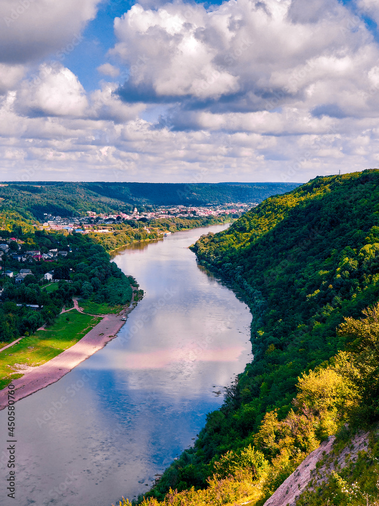 Large river flows in a green valley with wooded hills. Town on the ...