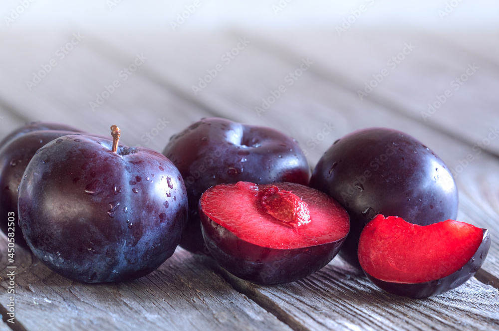 Round plums on a table with a cut and red pulp on a background of ...