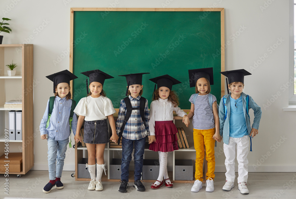 Group portrait of little kids in mortar boards in classroom. Elementary ...