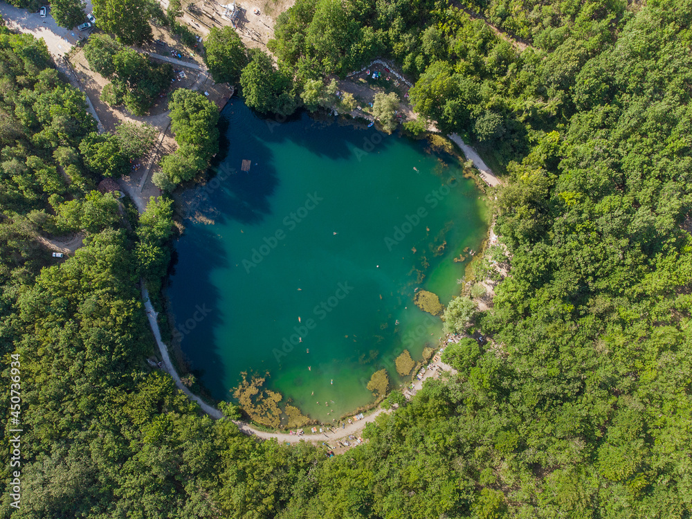Round small lake with clear water sorrounded by trees , overhead view ...