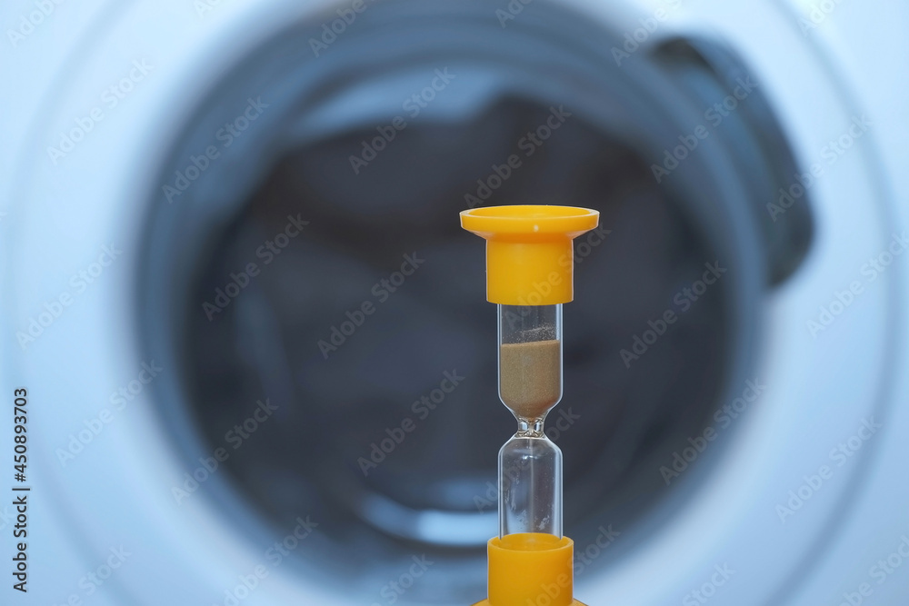 Yellow sandglass on window of washing machine with grey bedspread ...