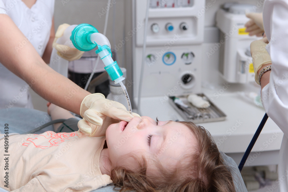 Little girl before surgery. The resuscitator holds an oxygen mask on ...