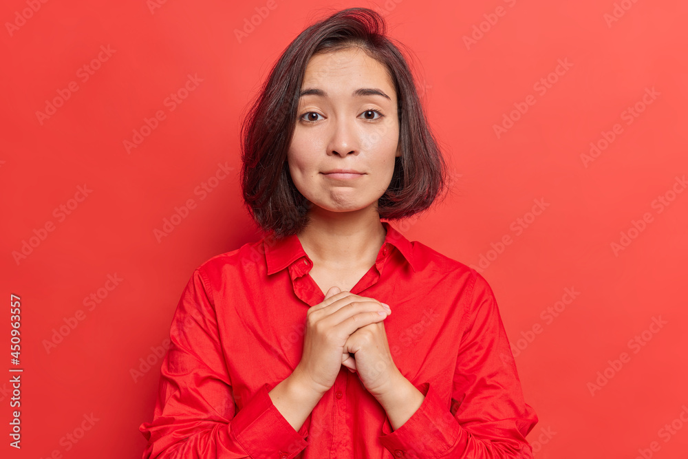 Hopeful good looking young Asian woman keeps hands together in pray ...