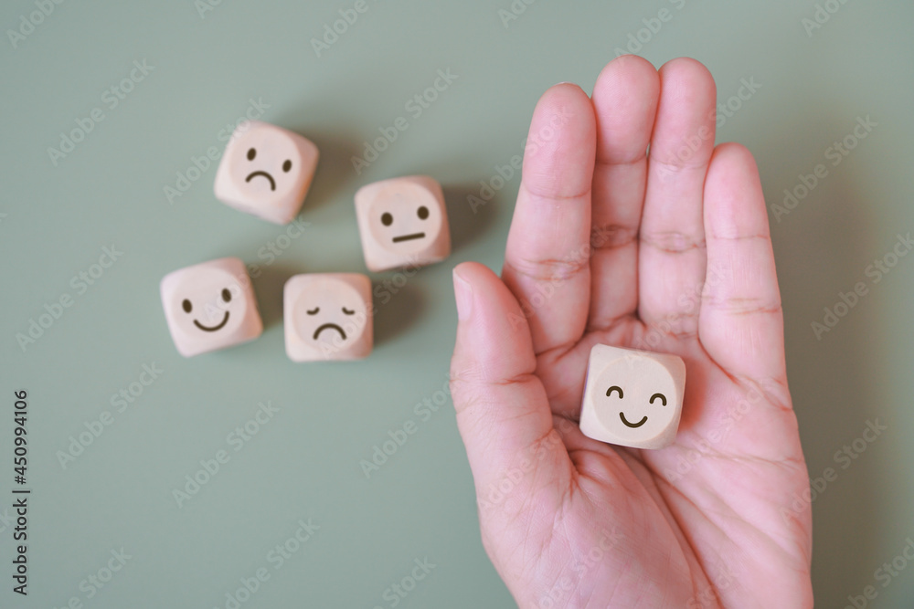 smiling face on wood cube in hand and blurred other face icon on green ...