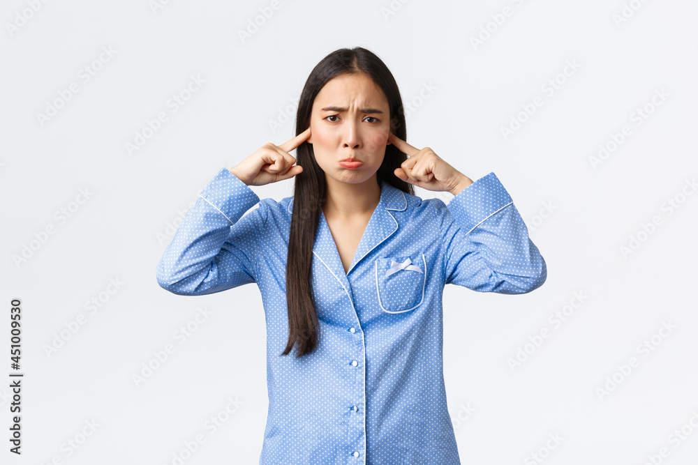 Timid and sad asian girl in blue pajamas pouting and whining, shut ears ...