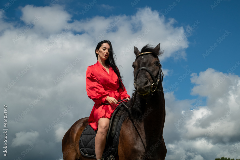 Young girl in long scarlet red dress riding black horse across dry ...