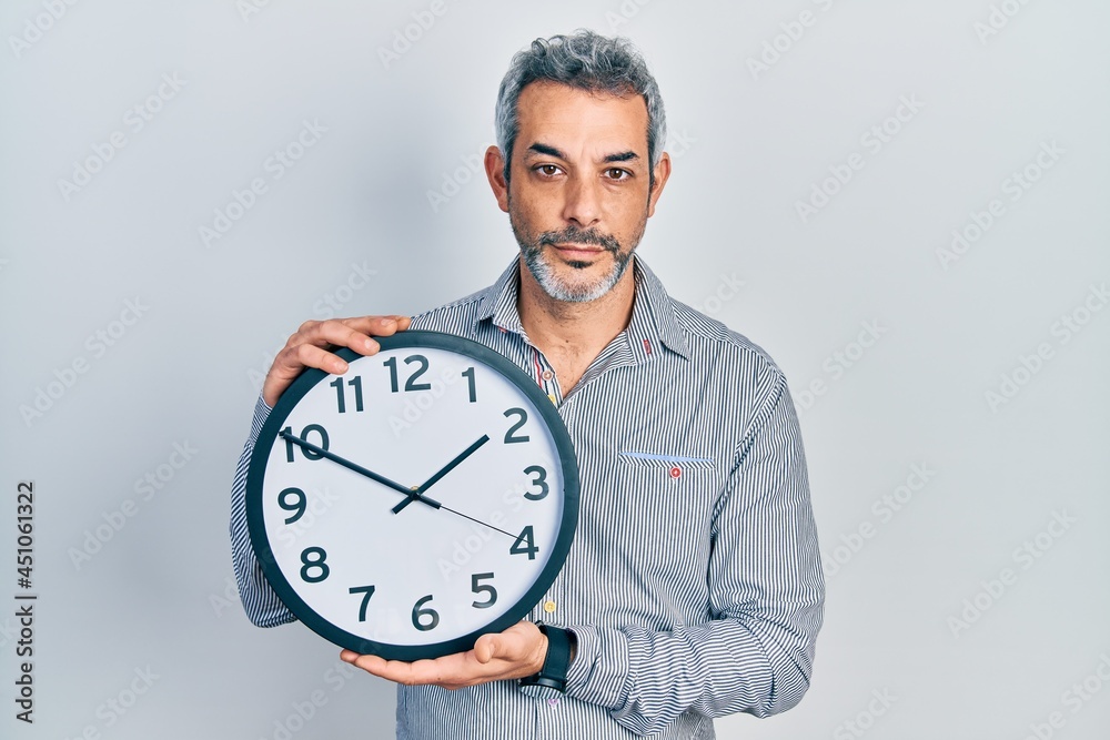 Handsome middle age man with grey hair holding big clock relaxed with ...