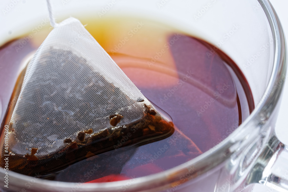 Wet tea bag - a pyramid of black tea is brewed in hot water in a ...