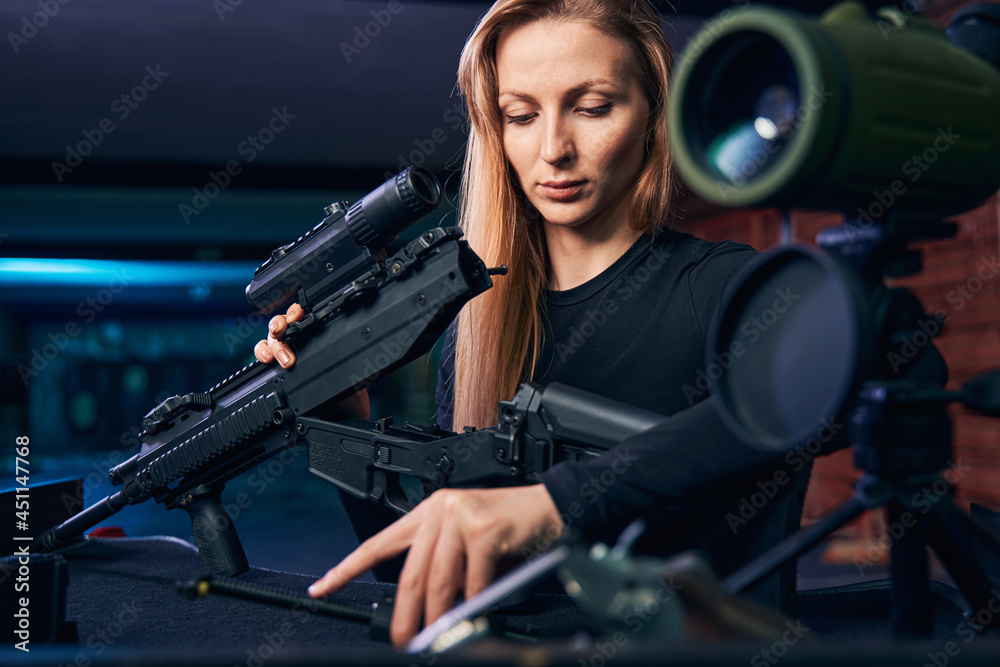 Concentrated beautiful long-haired female sniper assembling a weapon ...