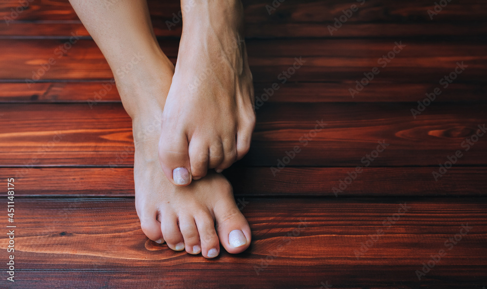Female feet on a brown wooden floor background close up. Itching and ...