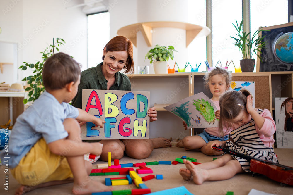 Group of small nursery school children with teacher on floor indoors in ...