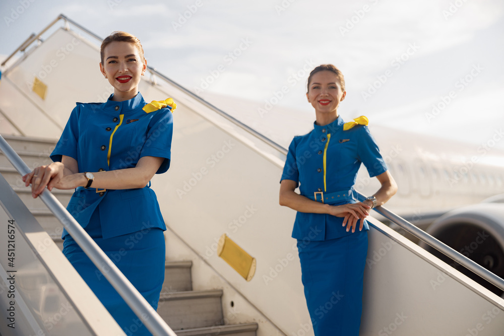 Two beautiful air stewardesses in blue uniform smiling at camera ...
