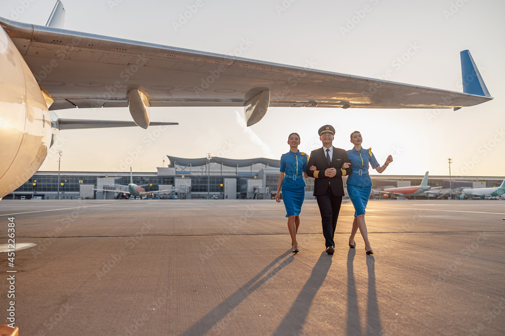 Full length shot of excited male pilot walking together with two female ...