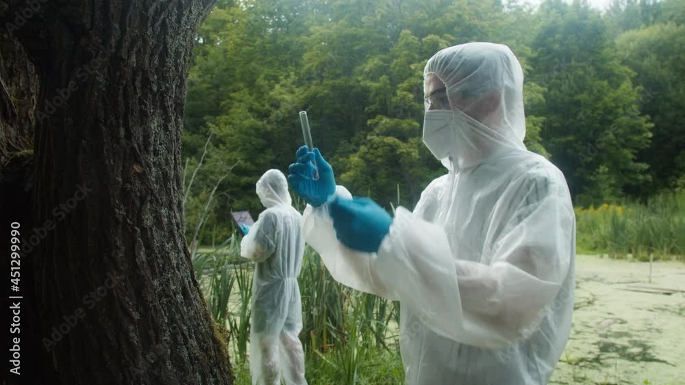 Chemists wearing ppe suits taking sample of tree bark for researching ...