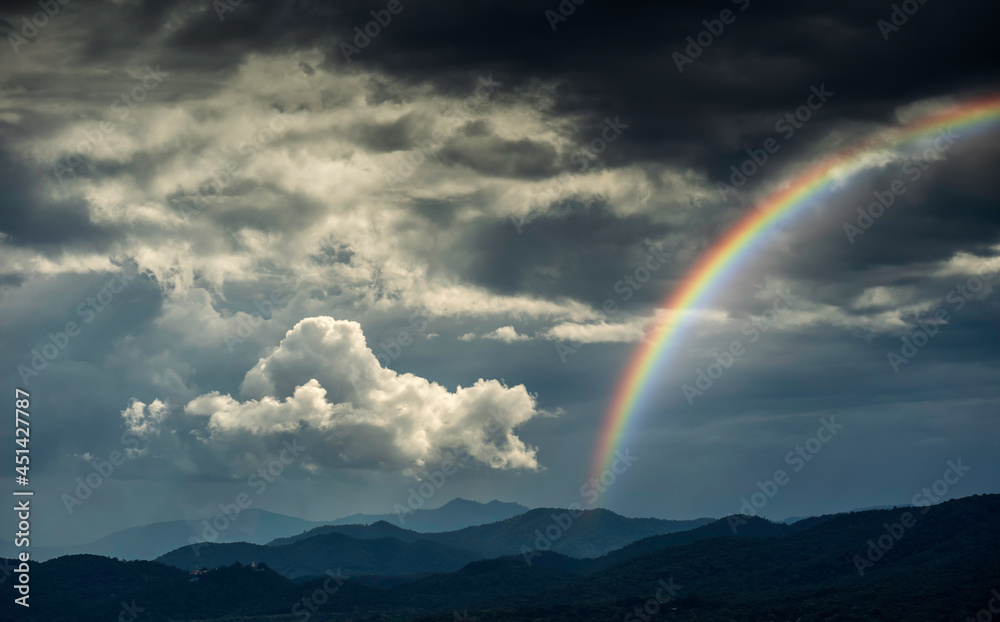 Colorful rainbow against dark storm clouds in background, A natural phenomenon that you can ...